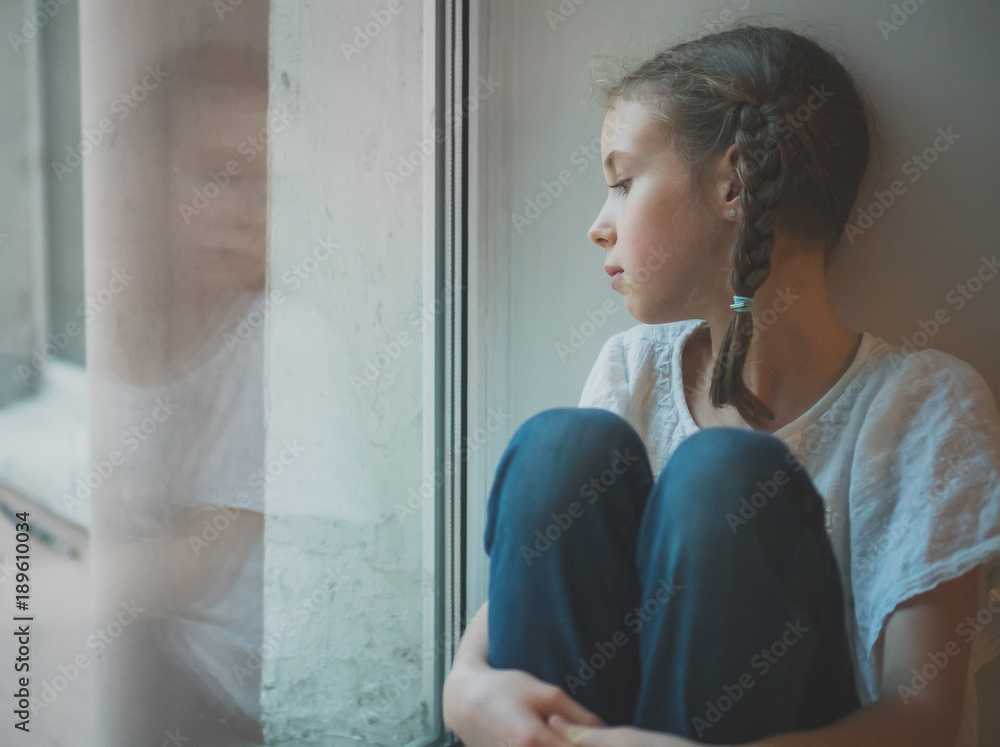 Sad little girl sitting near the window. Stock Photo | Adobe Stock