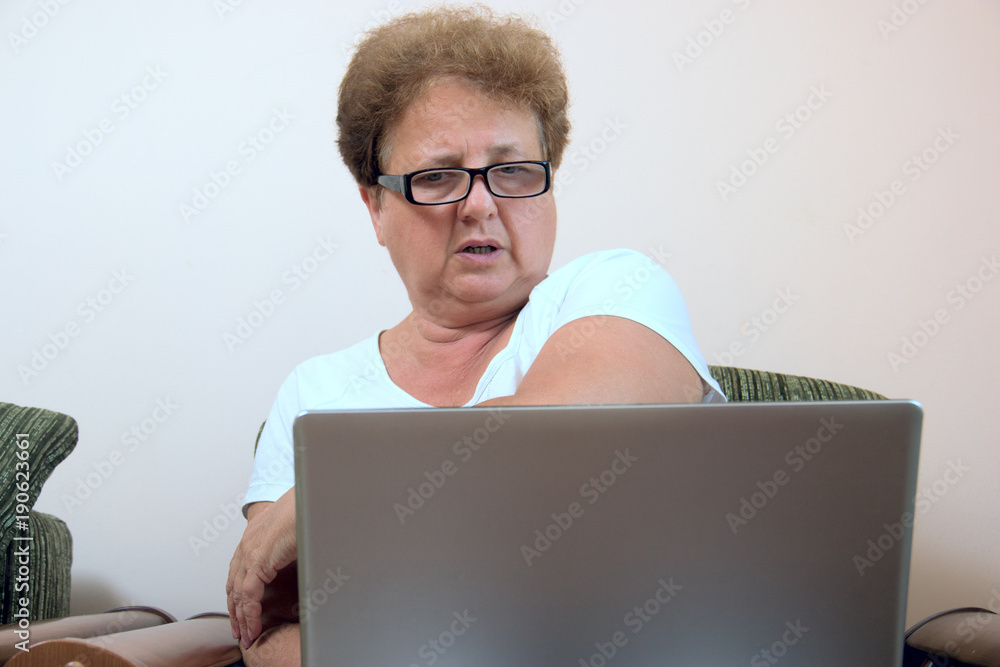 old woman looks frightened at the laptop screen. Grandmother does not ...