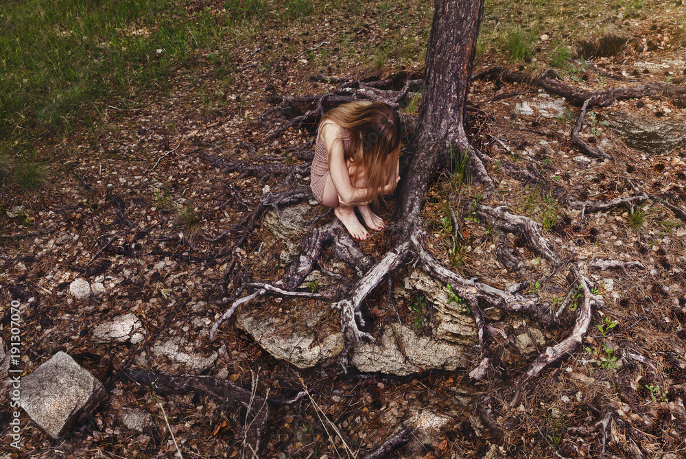 girl sitting near tree roots. The girl hid her face under hair, a girl ...