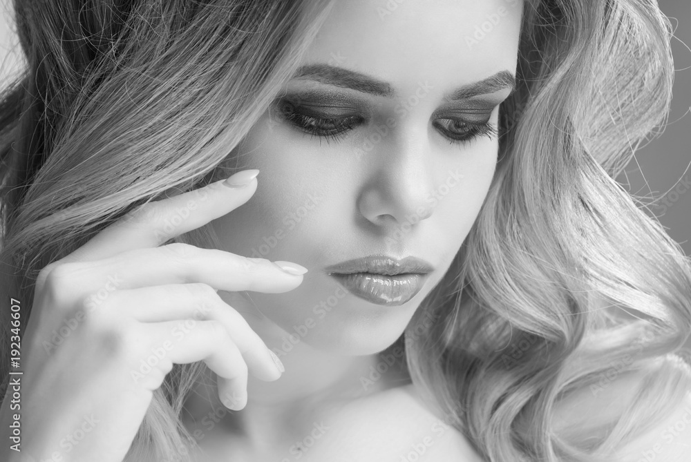 Blonde girl with makeup smoky eyes and curled hair looks down and holds ...