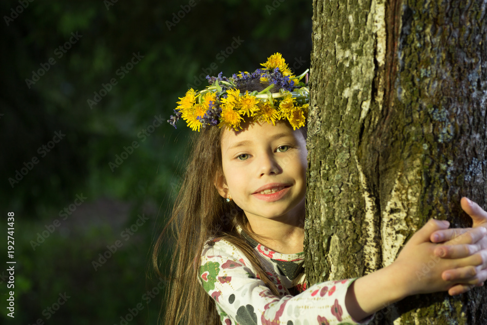 Cute girl in flowers wreath is looking out of birch tree in forest. The ...