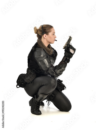 full length portrait of female wearing black tactical armour, crouching ...