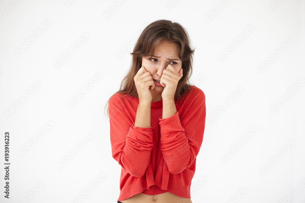 Unhappy frightened young woman in red top holding hands at her face ...