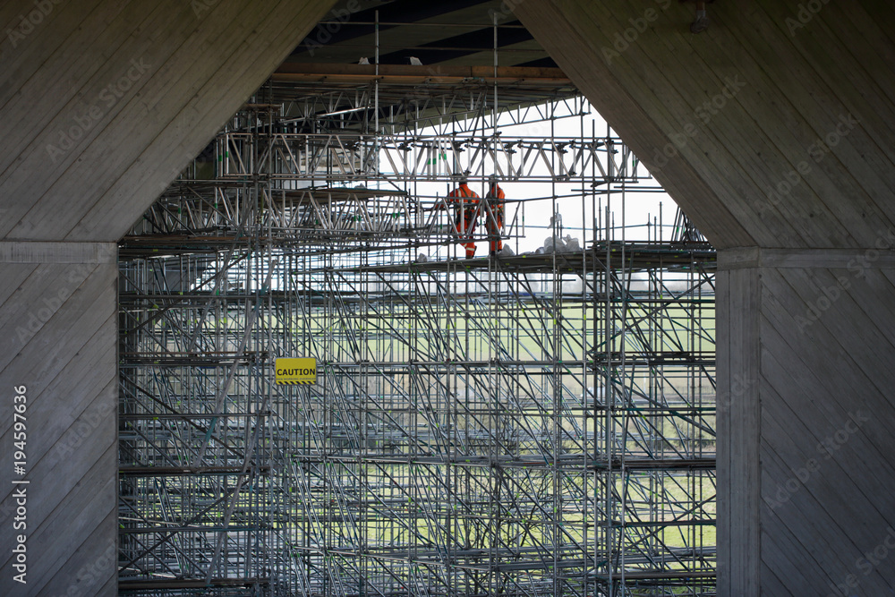 Highway maintenance. Two workers standing high up on a huge scaffolding ...