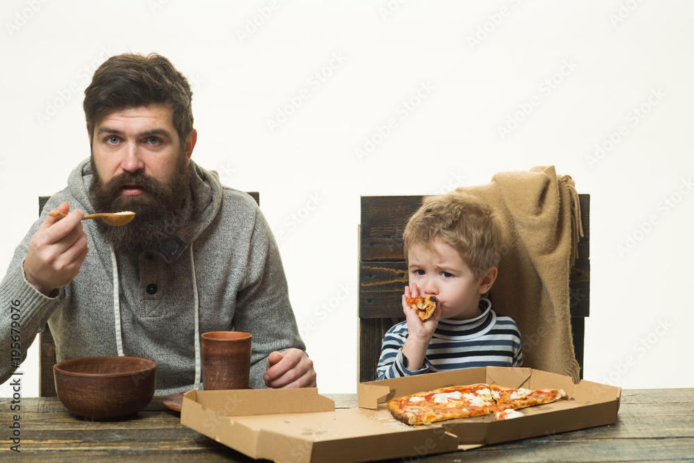 Sad hungry boy with daddy eats pizza at a wooden table in an Italian ...