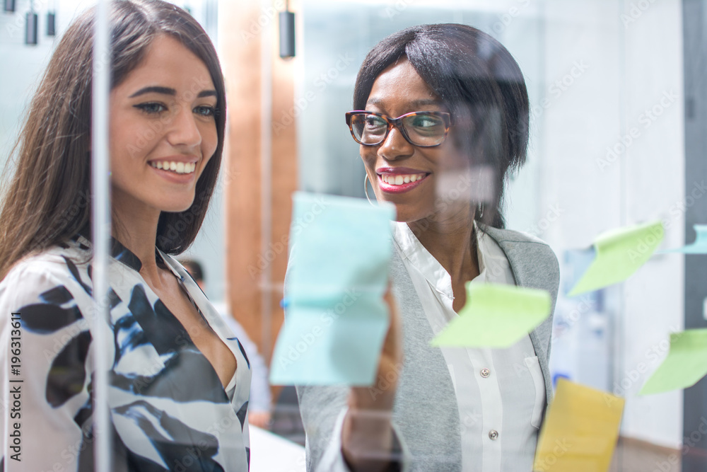 Portrait of two smiling women discussing ideas and brain storming with ...