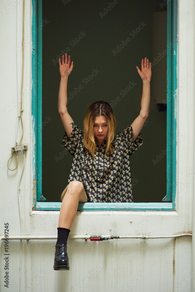 Girl in unglazed window with arms up and leg over frame. Stock Photo ...