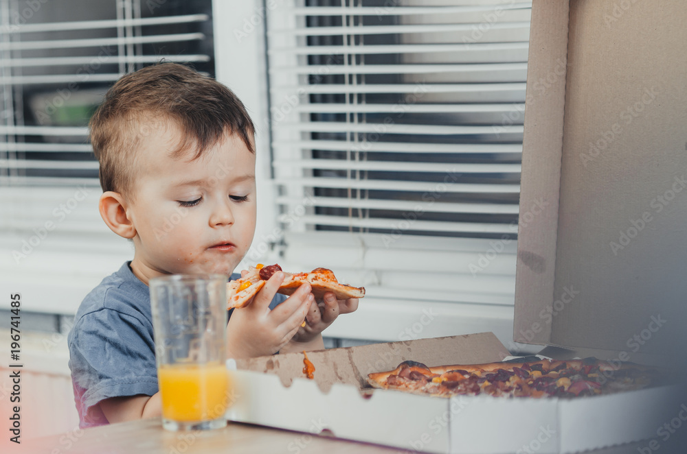 the little boy eats a huge harmful pizza himself in the kitchen and ...