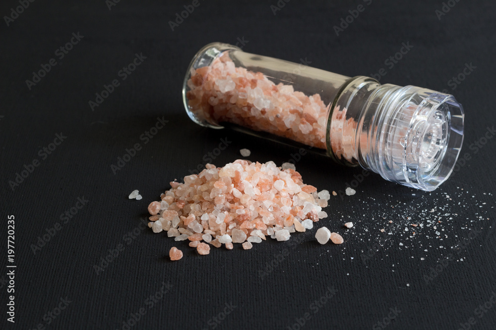 Salt on black background with commercial salt grinder and heap of pink ...