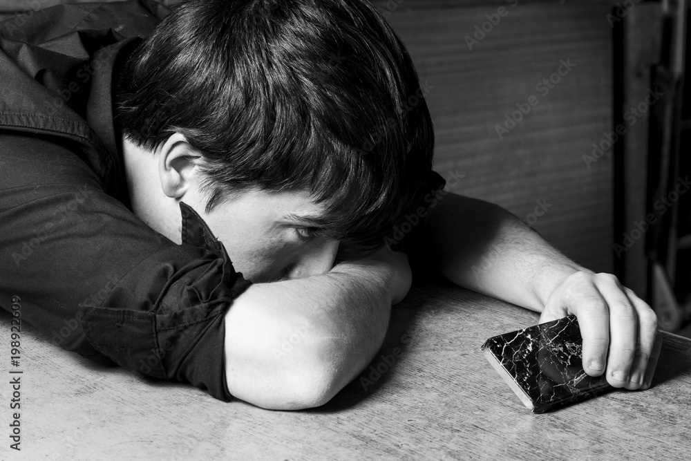Worried man laying on a table, looking to his smart phone. Bad news and ...
