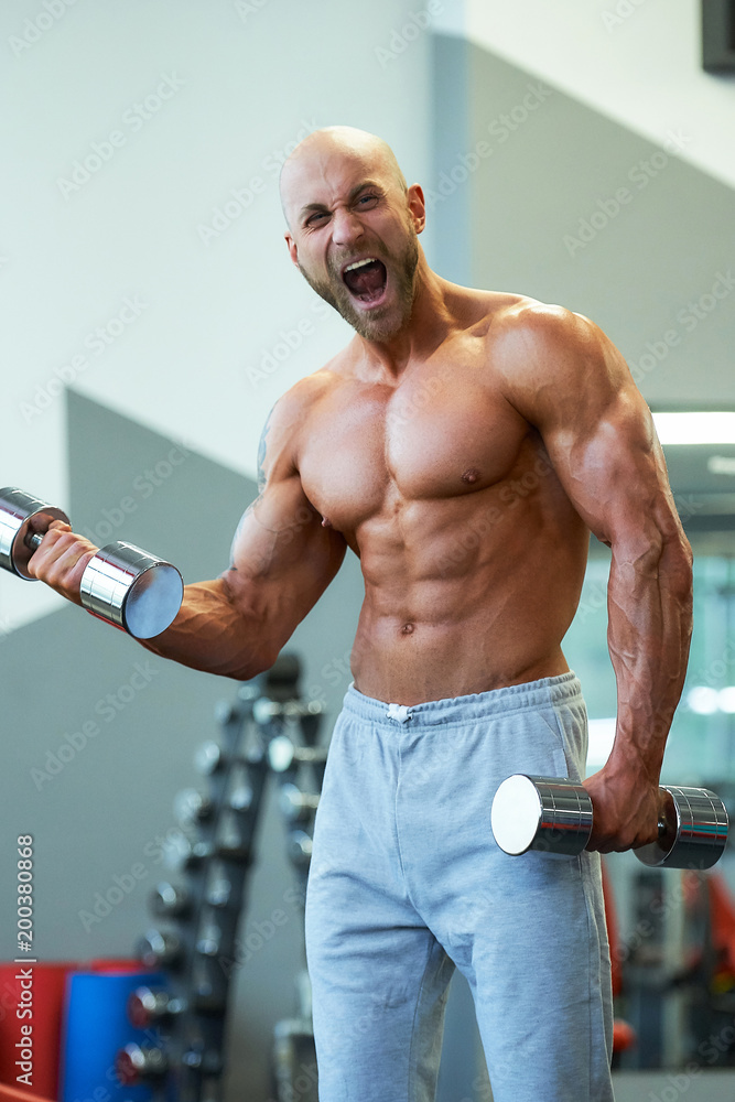 Shredded shirtless fit man with beard and shaved head doing biceps ...