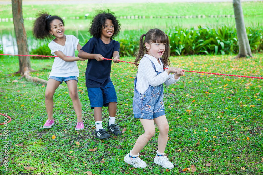 Happy kids or children pulling rope and playing tug of war at the park ...