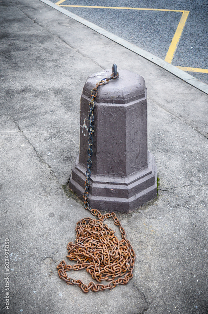 Concrete roadside traffic control bollard with rusty chain on asphalt ...