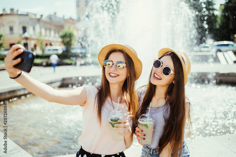 Beautiful female friends pose at camera of modern smart phone, make ...