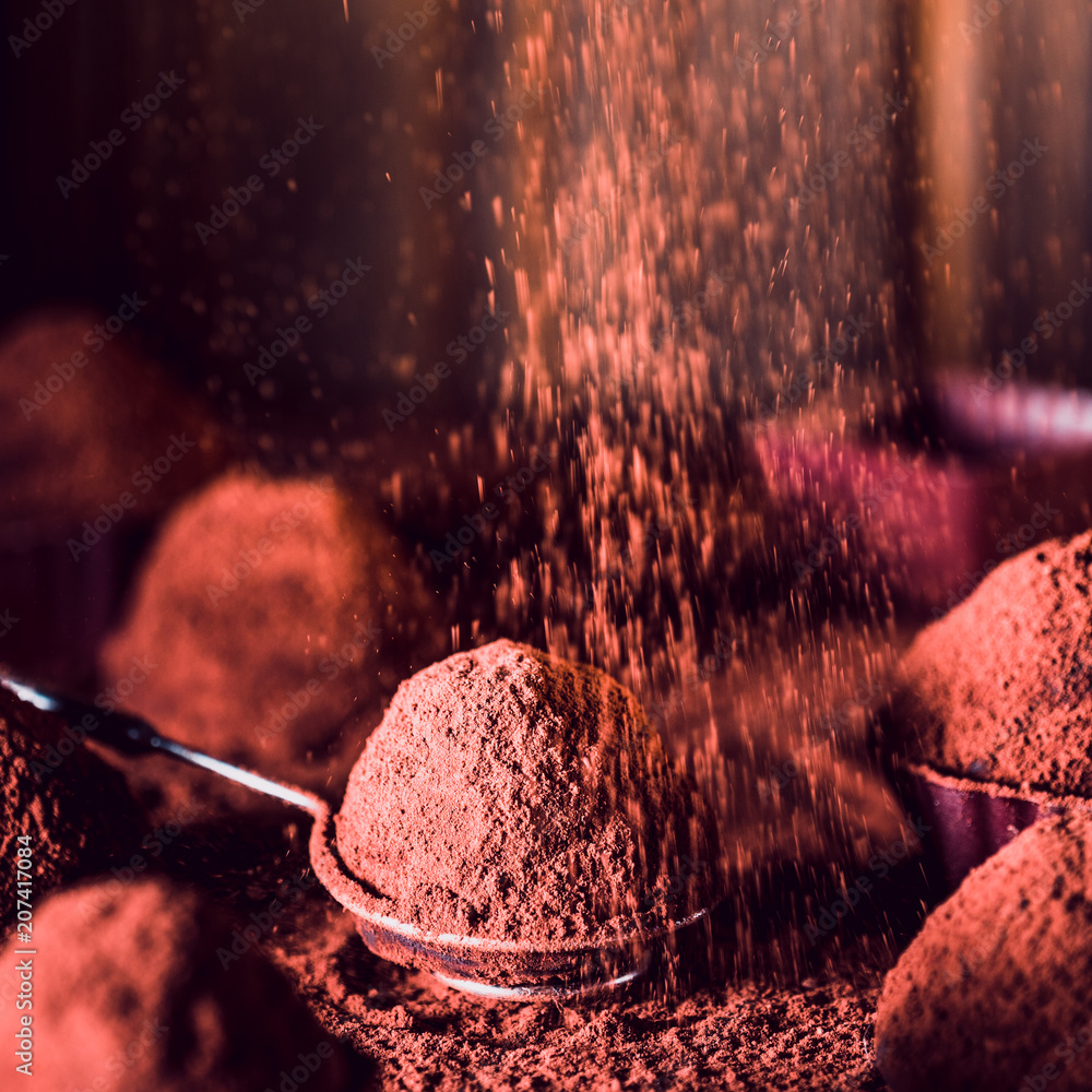 Chocolate truffles and falling cocoa powder on wooden background, macro ...