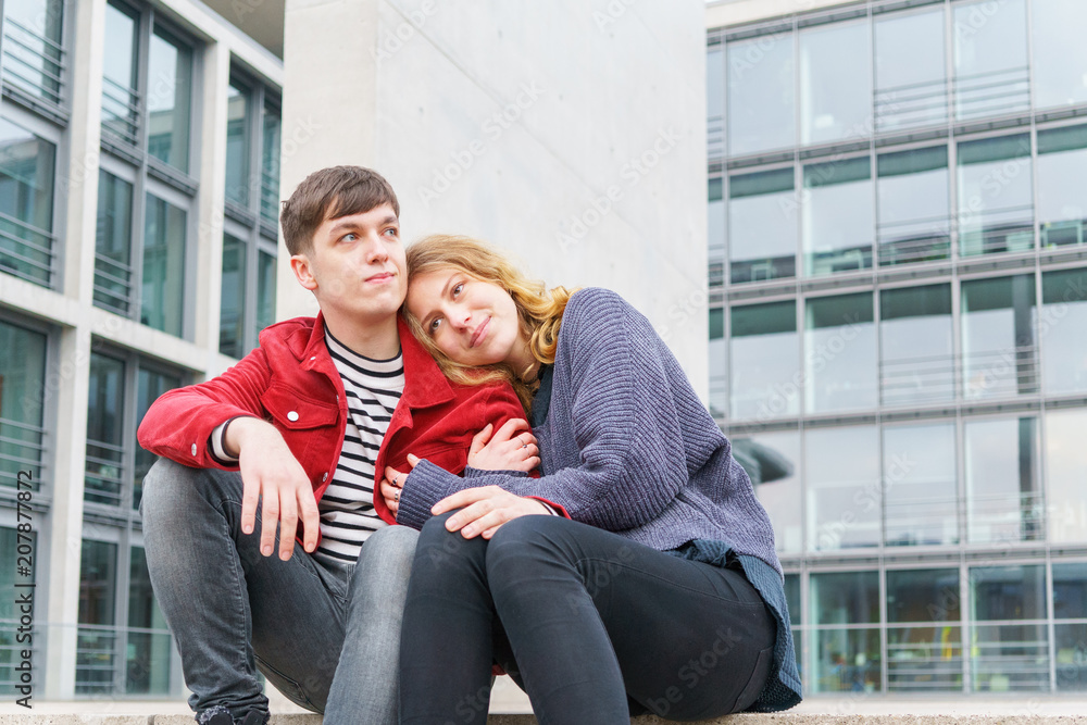 young affectionate heterosexual couple sitting on steps in front of ...