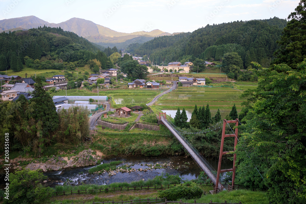 Small red suspension footbridge across river to rural Japanese farming ...