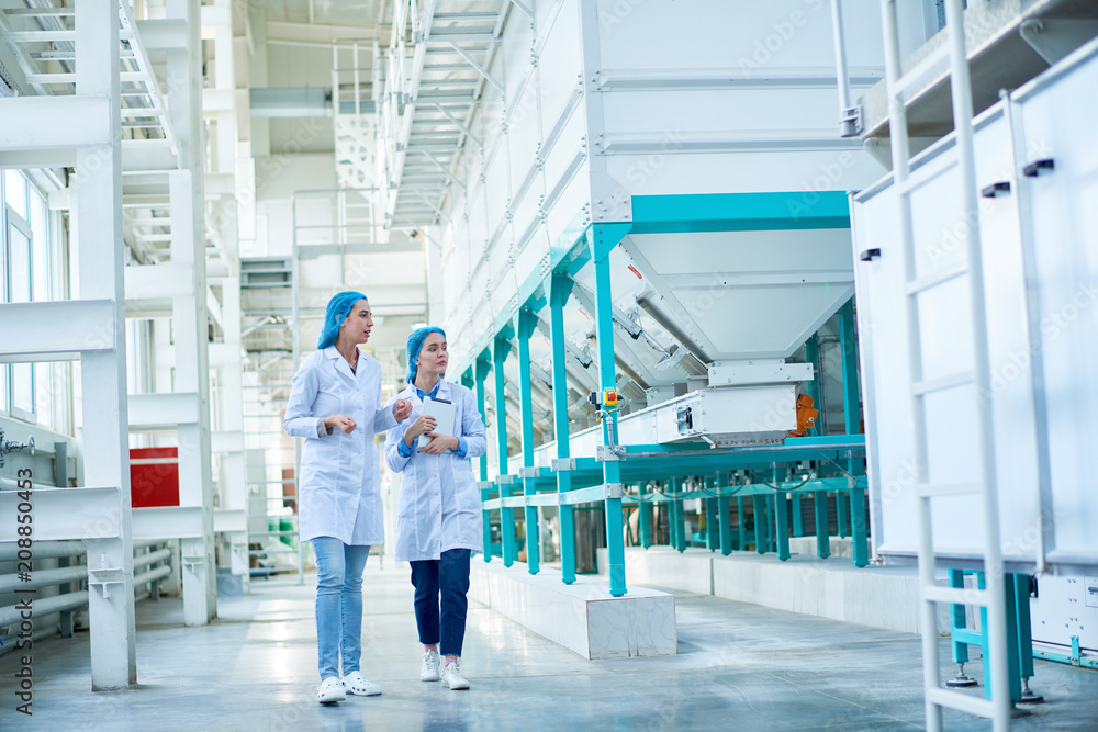 Full length portrait of two young female workers wearing lab coats ...