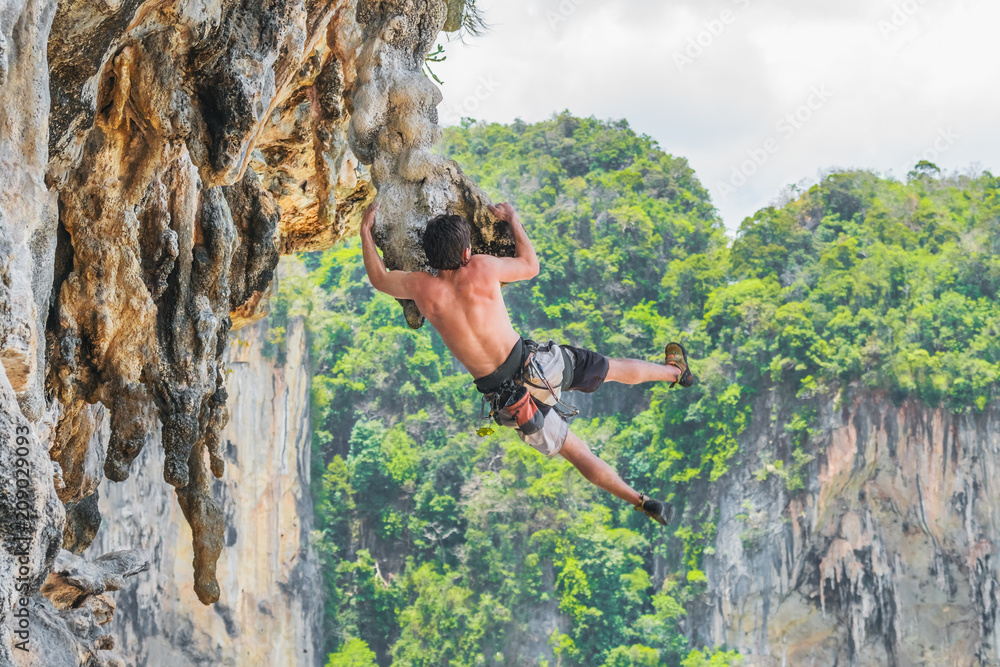 A young man hanging on a ledge of a cliff against the background of ...