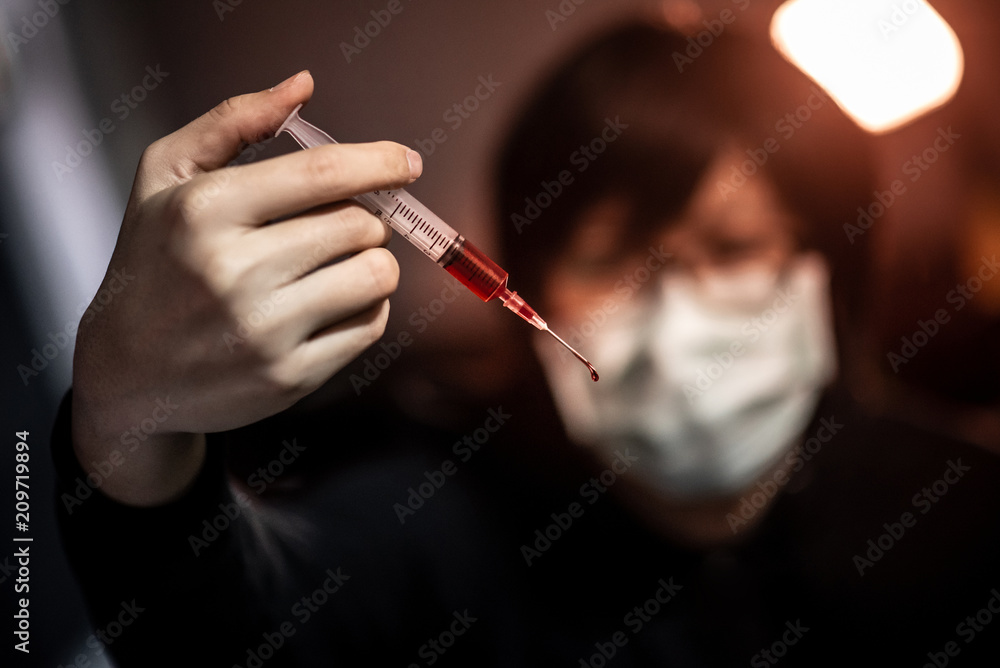 Young man in the mask using syringe for red drug injection. Drug abuse ...