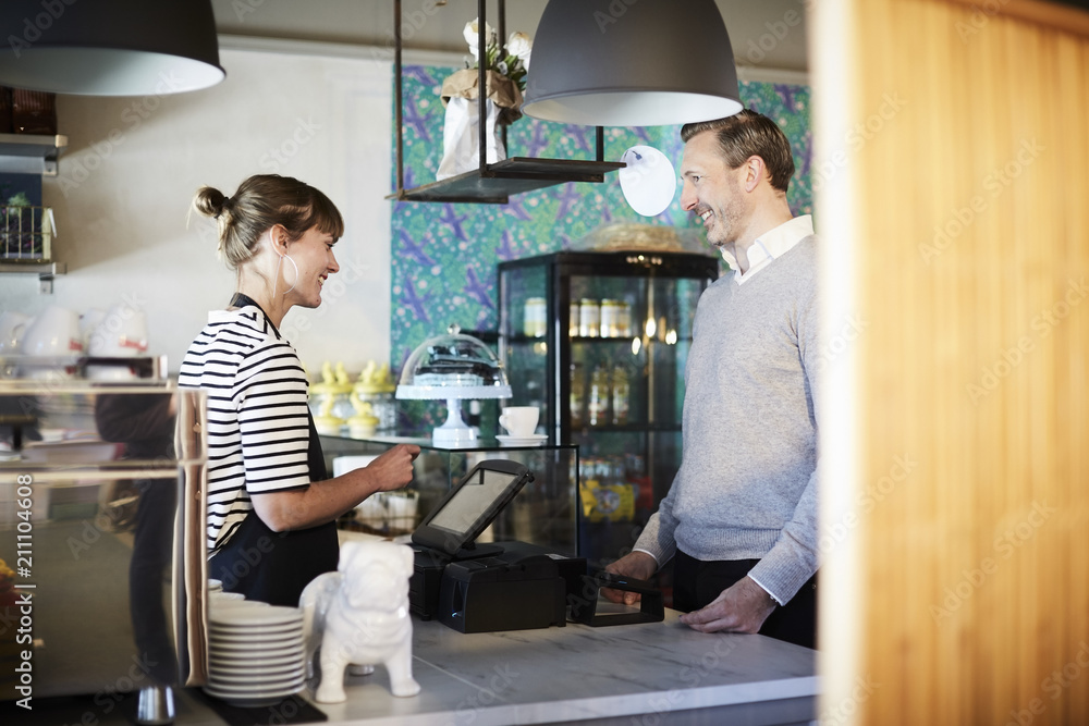 Smiling barista talking to customer while using cash register at ...