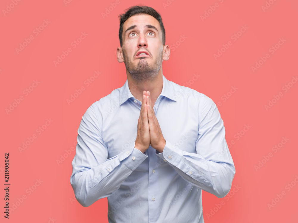 Handsome young businessman begging and praying with hands together with ...