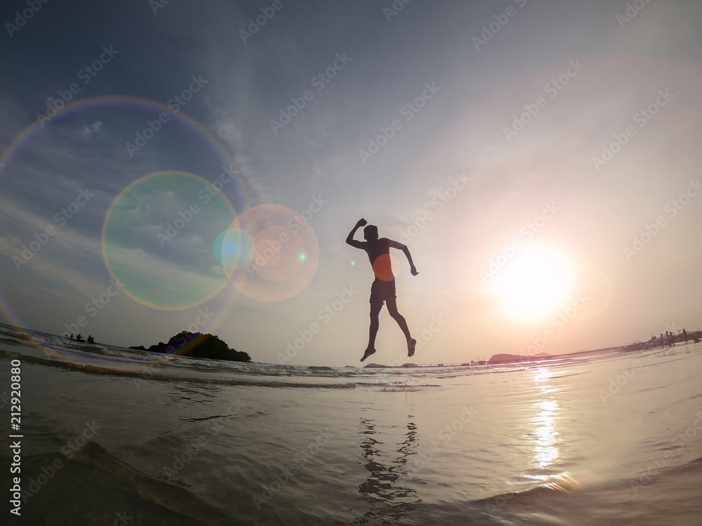 Silhouette Young Man jumping on the sea beach at sunset with lens flare ...