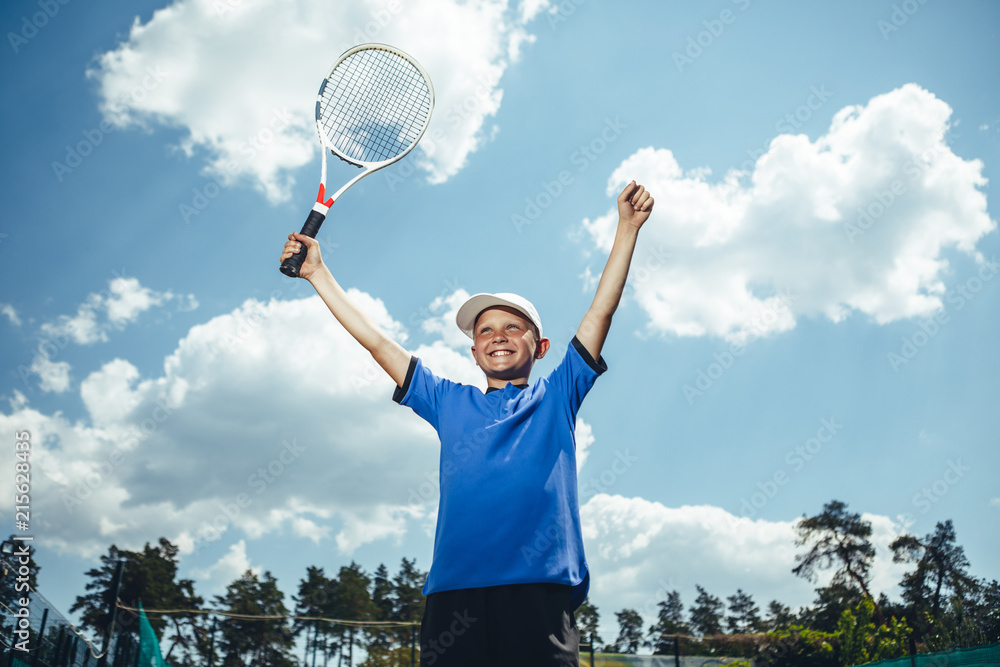 Low angle portrait of beaming kid with racket in arm expressing ...