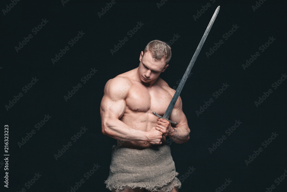 Bodybuilder man posing with a sword isolated on black background ...