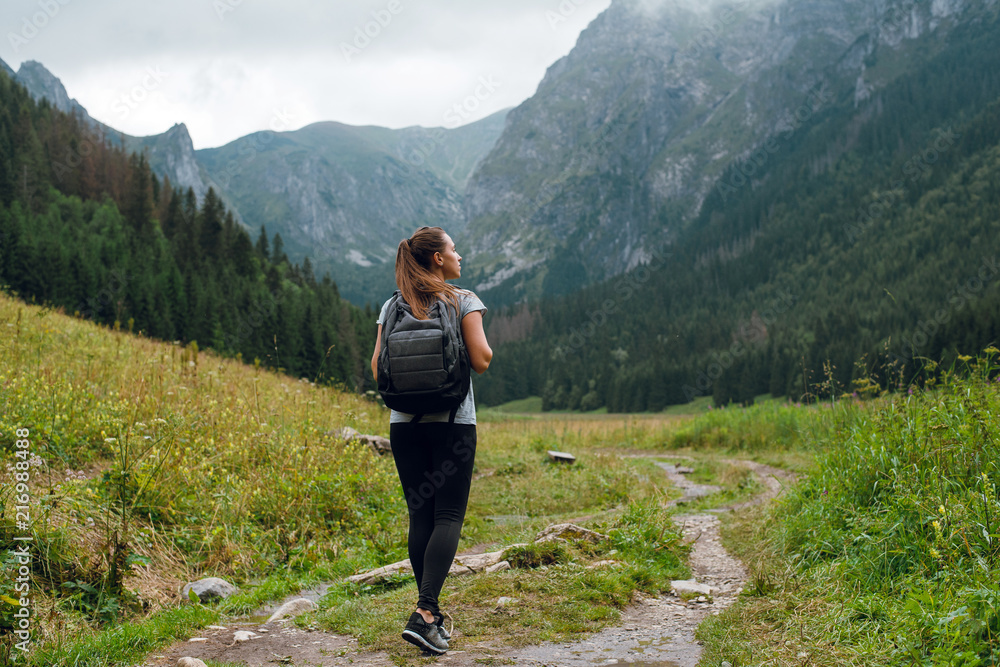 Rear shot of young brunette backpacker woman hiking on the green ...