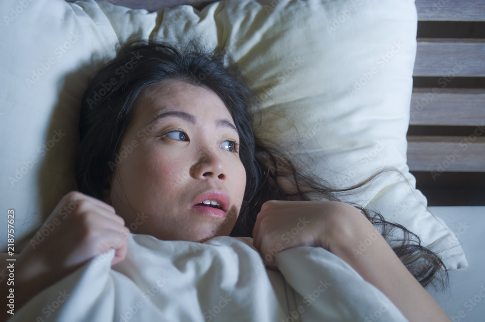 Foto de Stock young scared and stressed Asian Chinese woman lying in bed suffering nightmare in ...