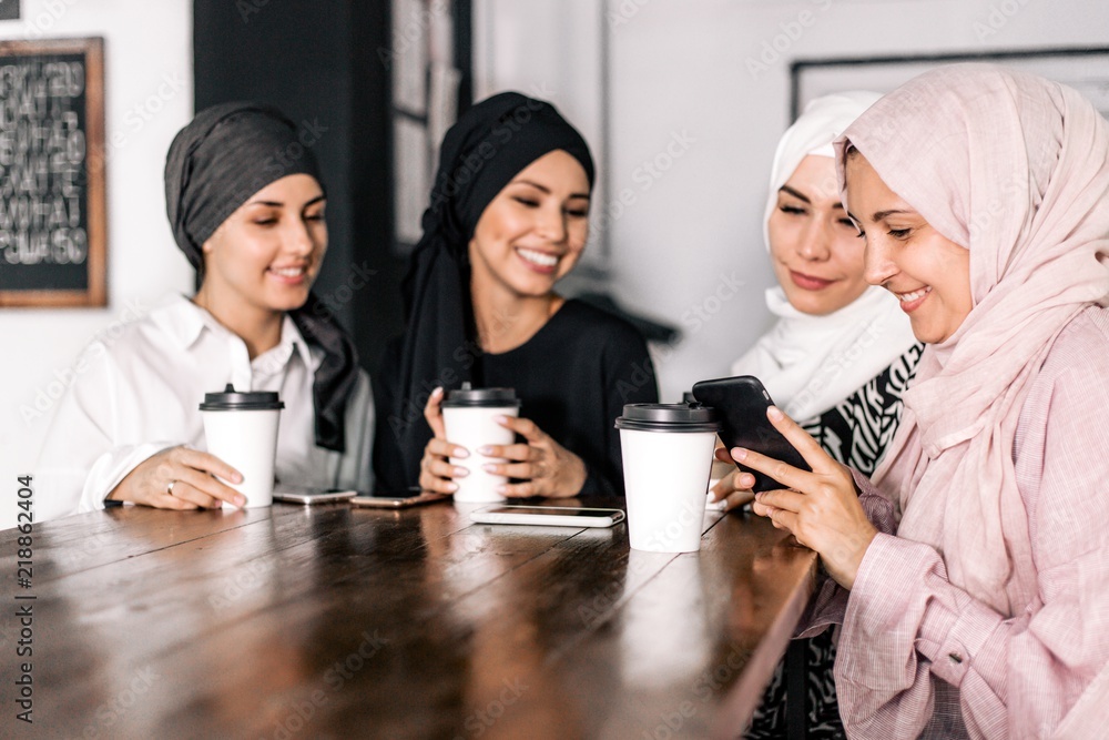 Four Muslim women hijab drinking coffee sitting at a table in a cafe ...