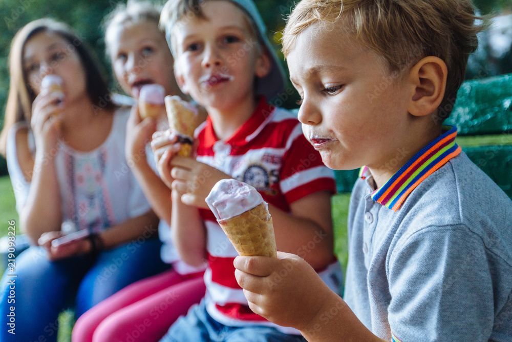 Team of four different age happy children eating ice-cream outdoors in ...