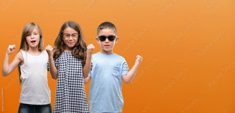 Group of boy and girls kids over orange background screaming proud and ...
