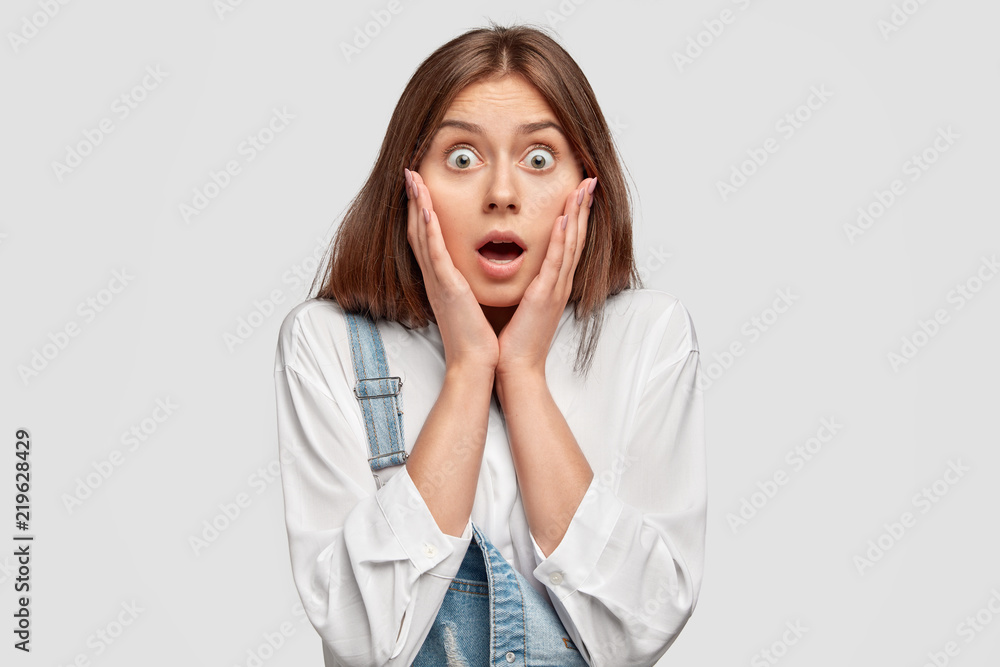 Foto de Stock Fearful frightened young female keeps hands on cheeks ...