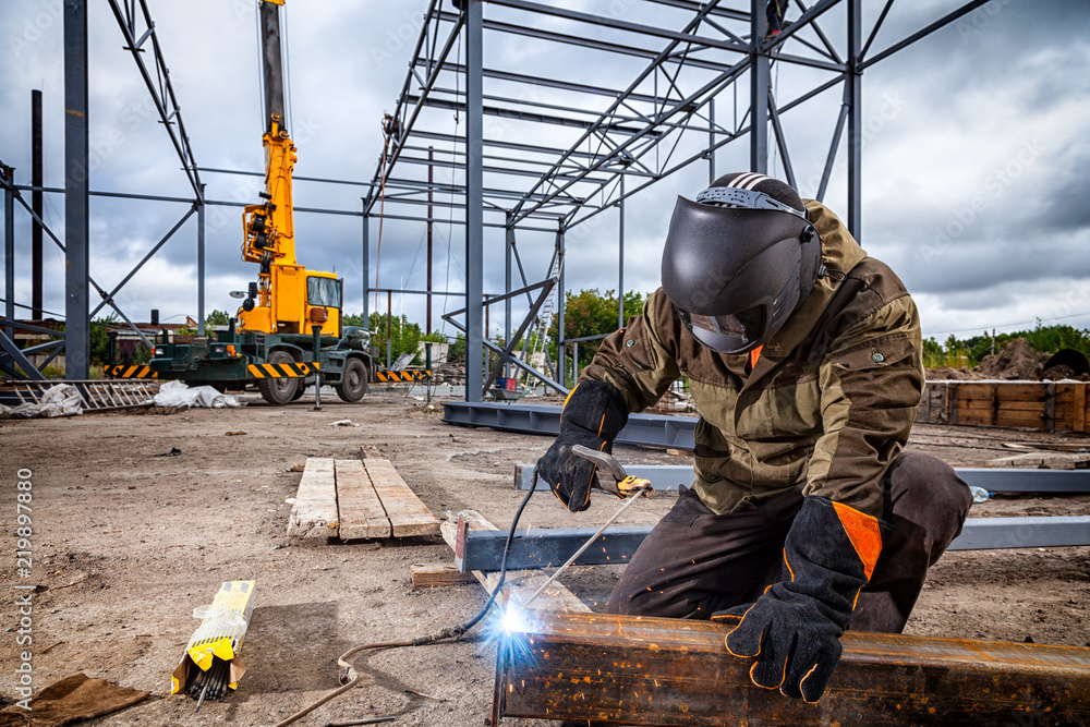 A young man welder in brown uniform, welding mask and welders leathers ...