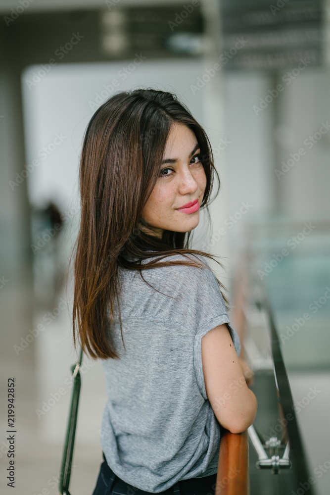 A young Japanese woman leans against the glass railing in a clean ...