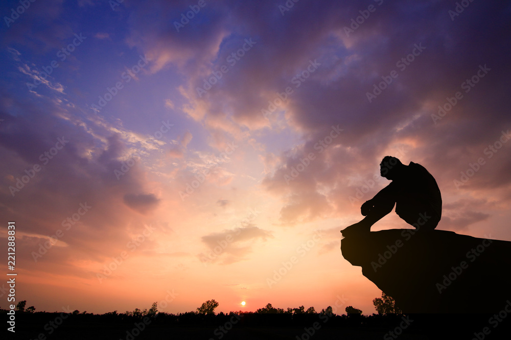Foto Silhouetted photo. Lonely man sitting on cliff. He is unhappy and ...