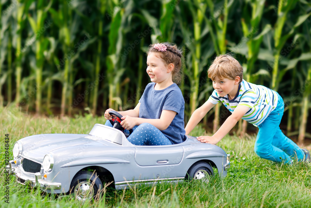 Two happy children playing with big old toy car in summer garden ...