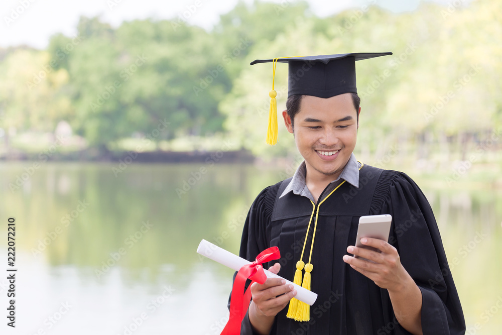 Happy graduated young man in cap and gown talking with parent in mobile ...