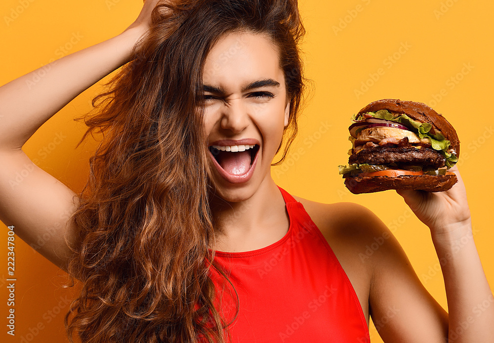 Woman hold big barbecue burger sandwich with hungry mouth happy screaming laughing on yellow ...