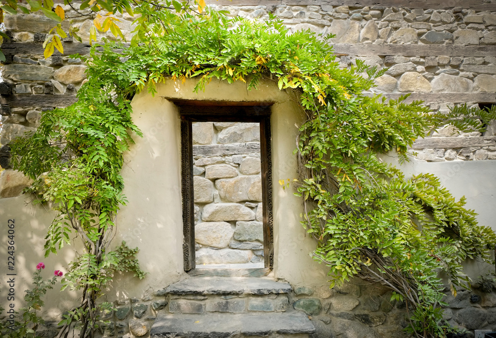 Wooden door frame gate covered with trees in front of stone retaining ...