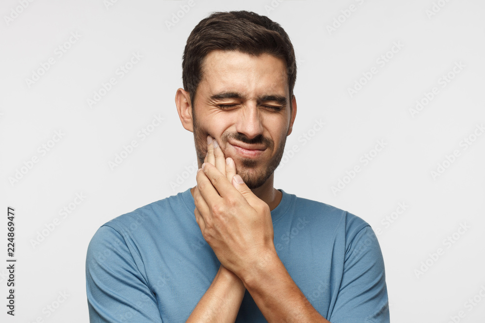Tooth ache. Young man feeling pain, holding his cheek with both hands ...