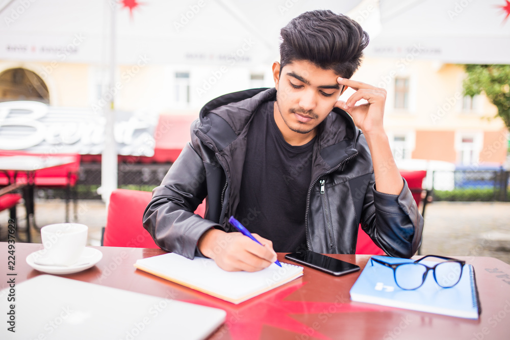 Young indian man freelancer of creative occupation writing down in ...
