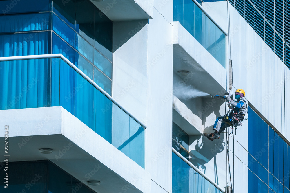 Worker wearing safety harness washes glass facade at height on modern ...