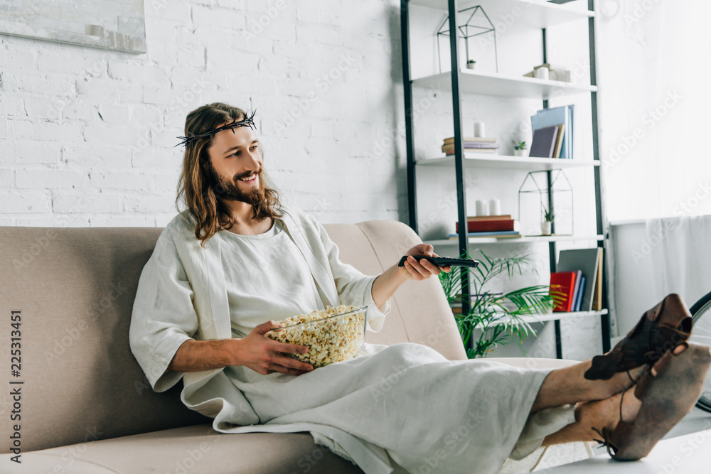 happy Jesus in crown of thorns watching tv and sitting with bowl of ...