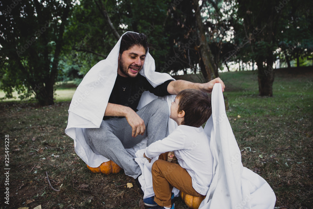 Father and son playing ghosts with white sheets in the garden ...