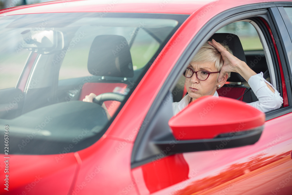 Annoyed mature woman sitting in a car, stuck in a traffic jam. Front ...