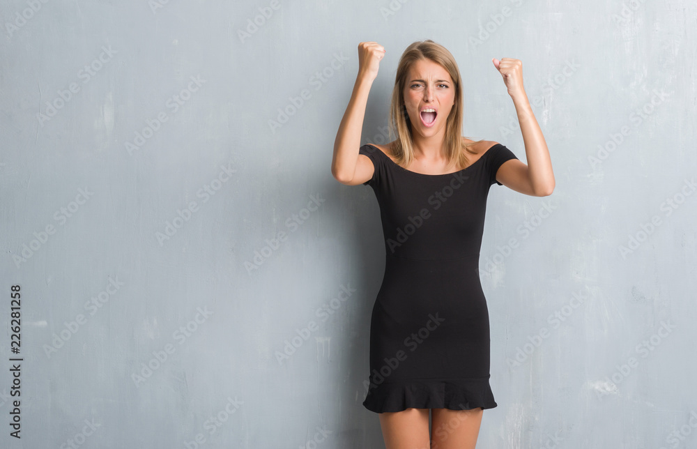 Beautiful young woman standing over grunge grey wall wearing elegant ...
