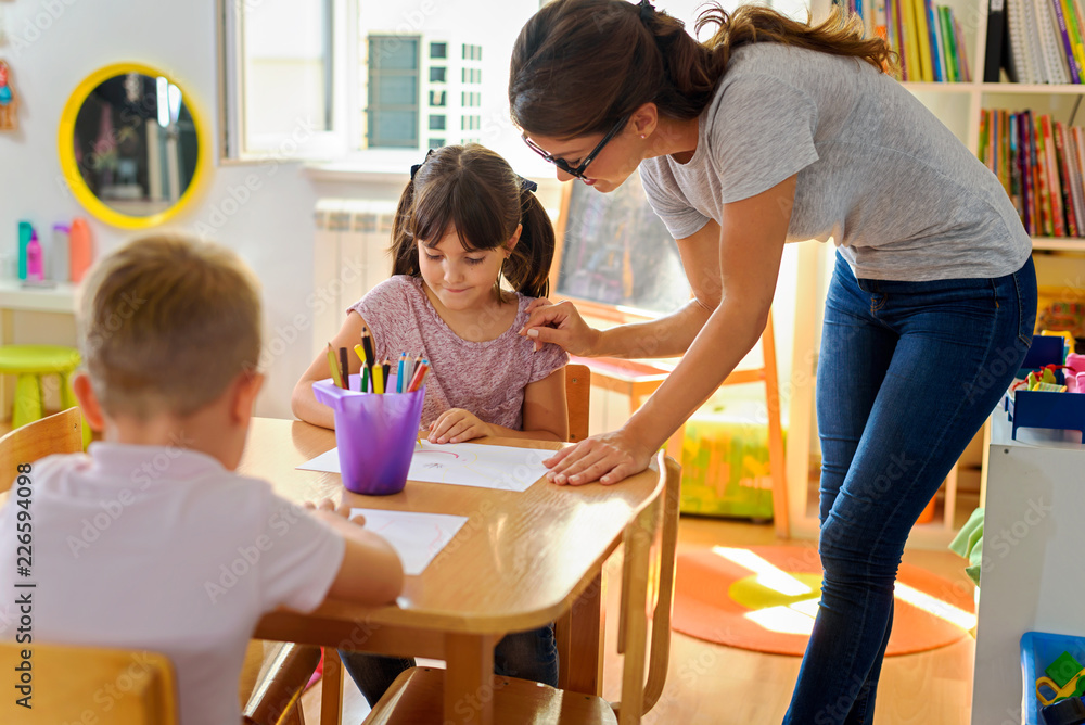 Preschool teacher assisting children with their drawings. Early ...